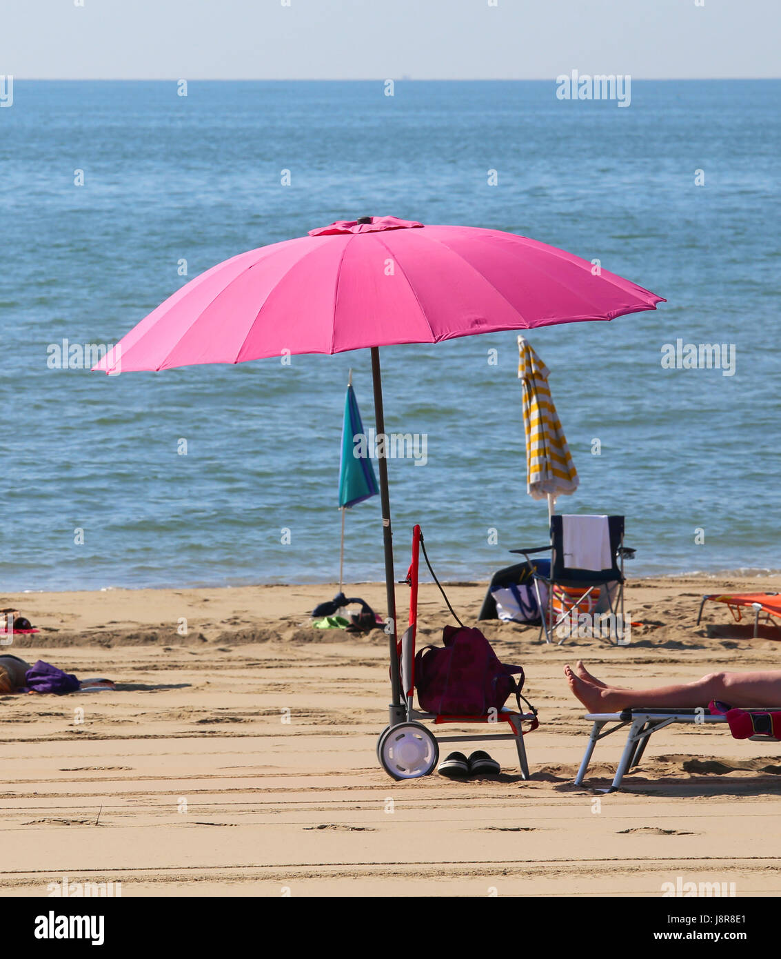 Large parasol and the feet of an elderly man sunbathing on the beach in ...