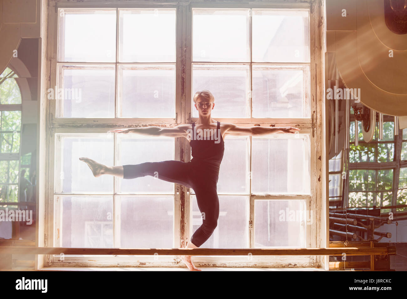 Male ballet dancer is dancing in front of a large window, standing on ...