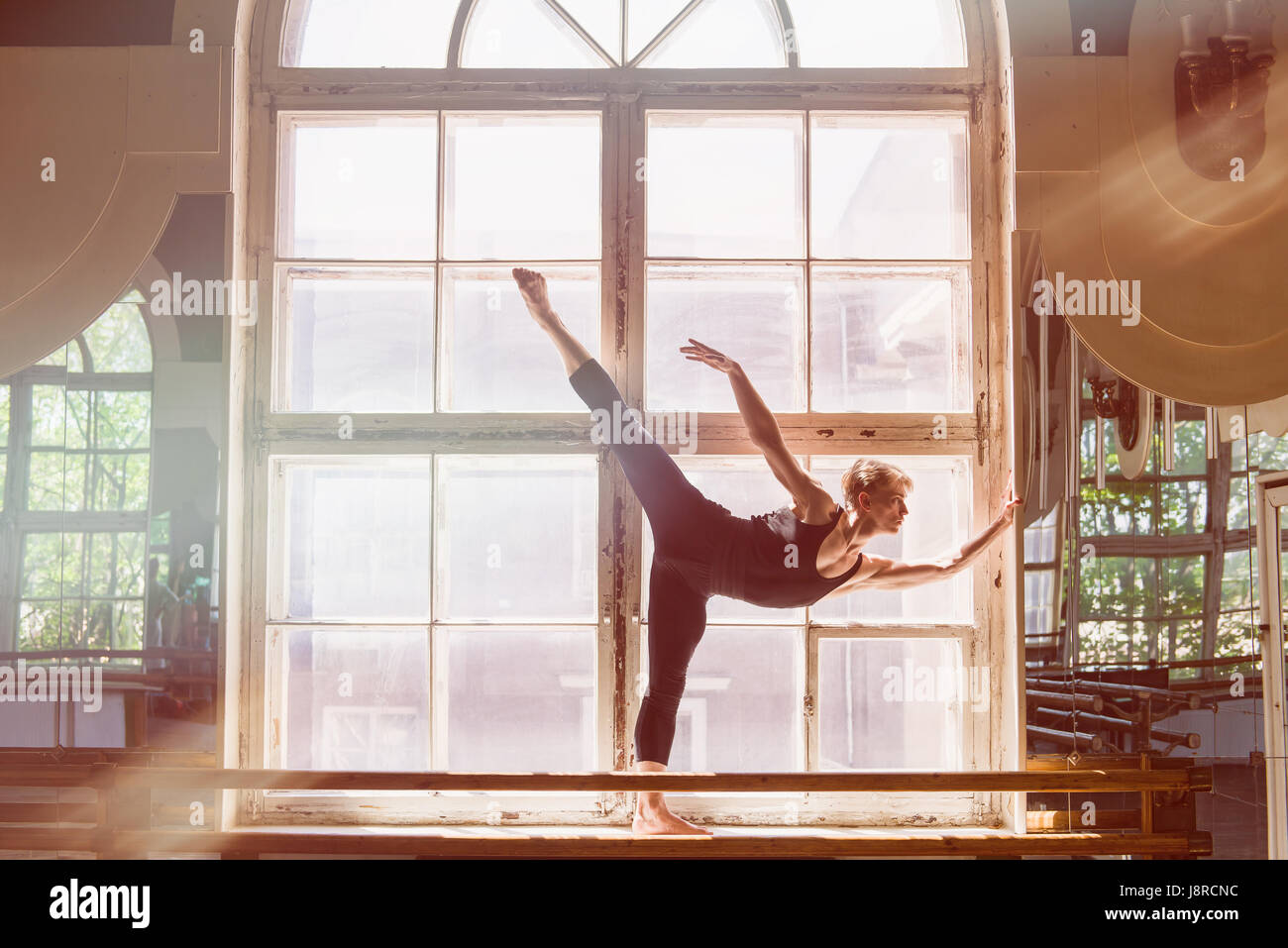 Male ballet dancer is dancing in front of a large window, standing on ...
