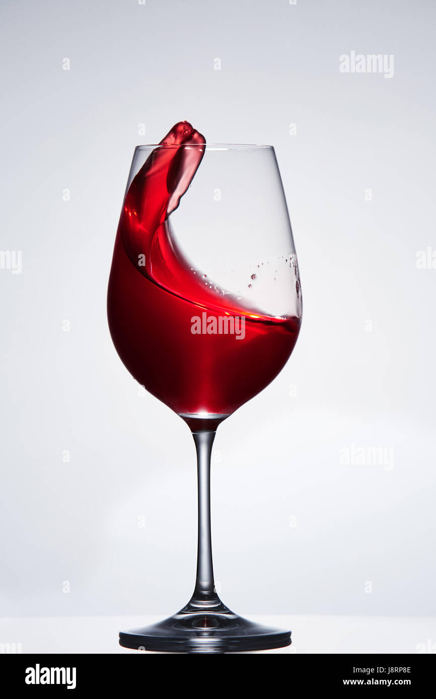 Splashing and moving red wine in the pure wineglass standing against ...