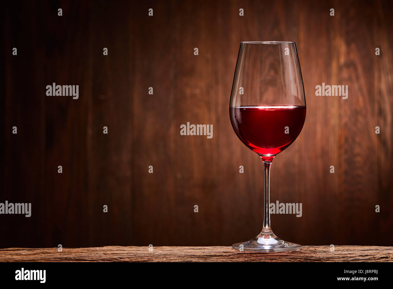 Fragile goblet of the red wine on the wooden stand on wooden wall ...