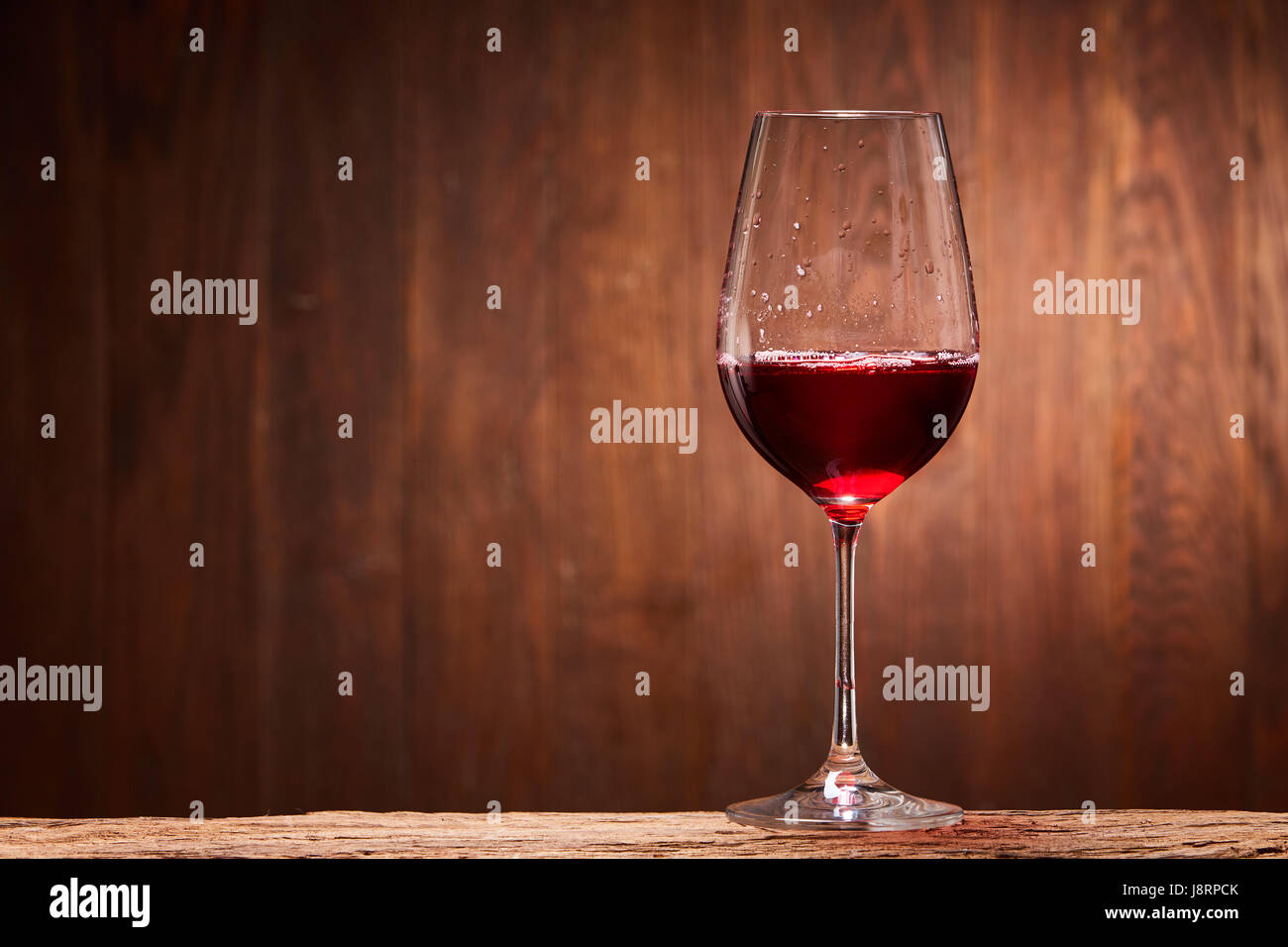 Fragile goblet of the red wine on the wooden stand on wooden wall ...
