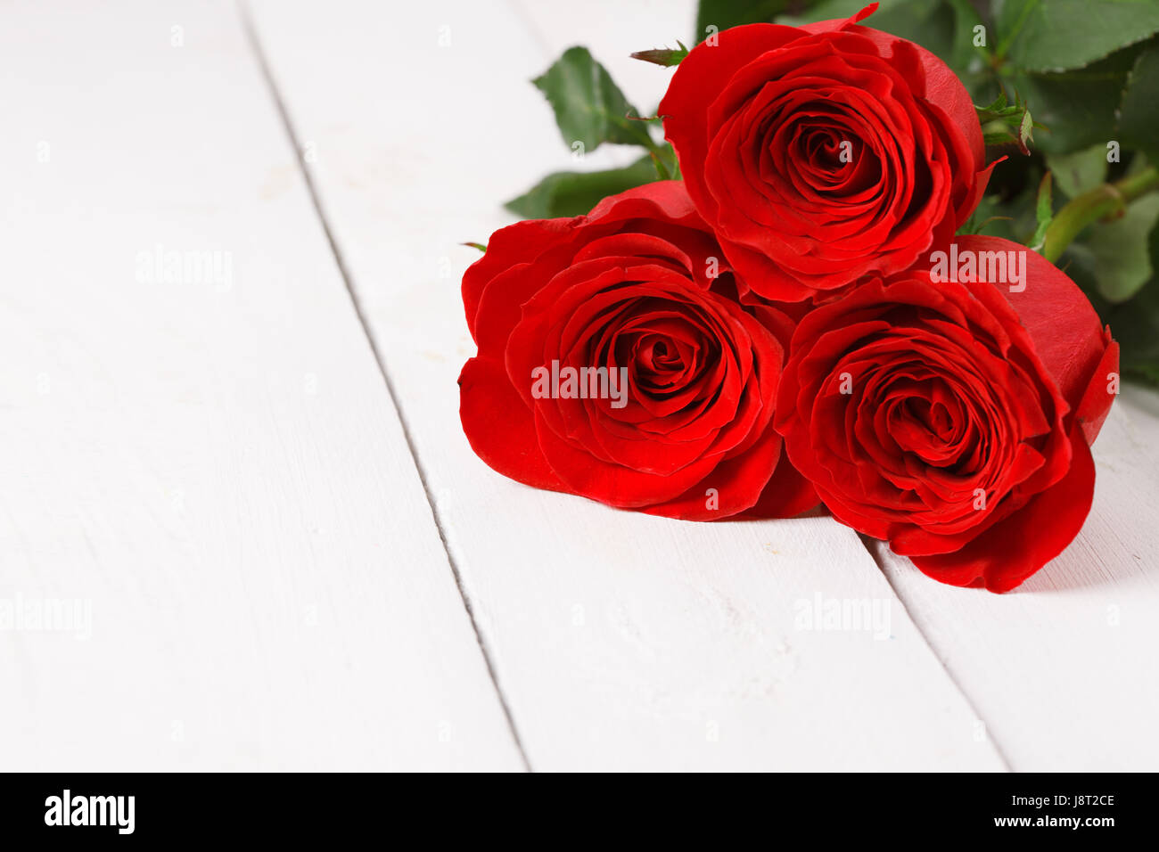 Three red roses lie on white table Stock Photo - Alamy
