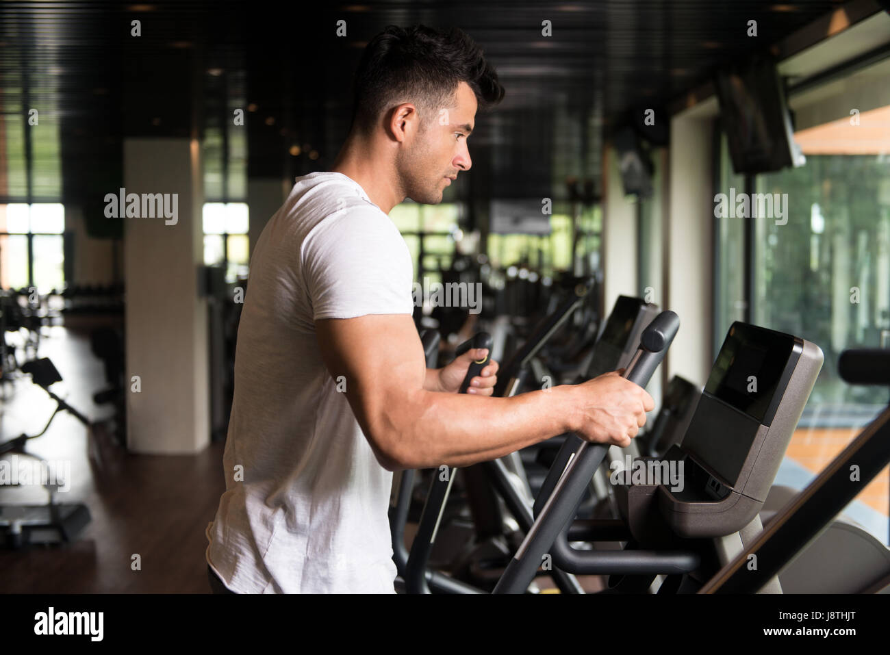Muscular Man Doing Aerobics Elliptical Walker In Modern Fitness Center ...