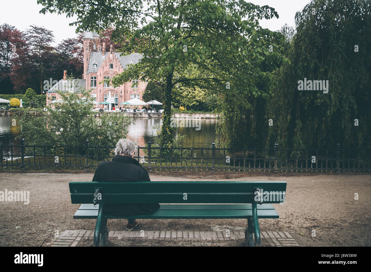 An old man sits on a green bench overlooking the water in ...