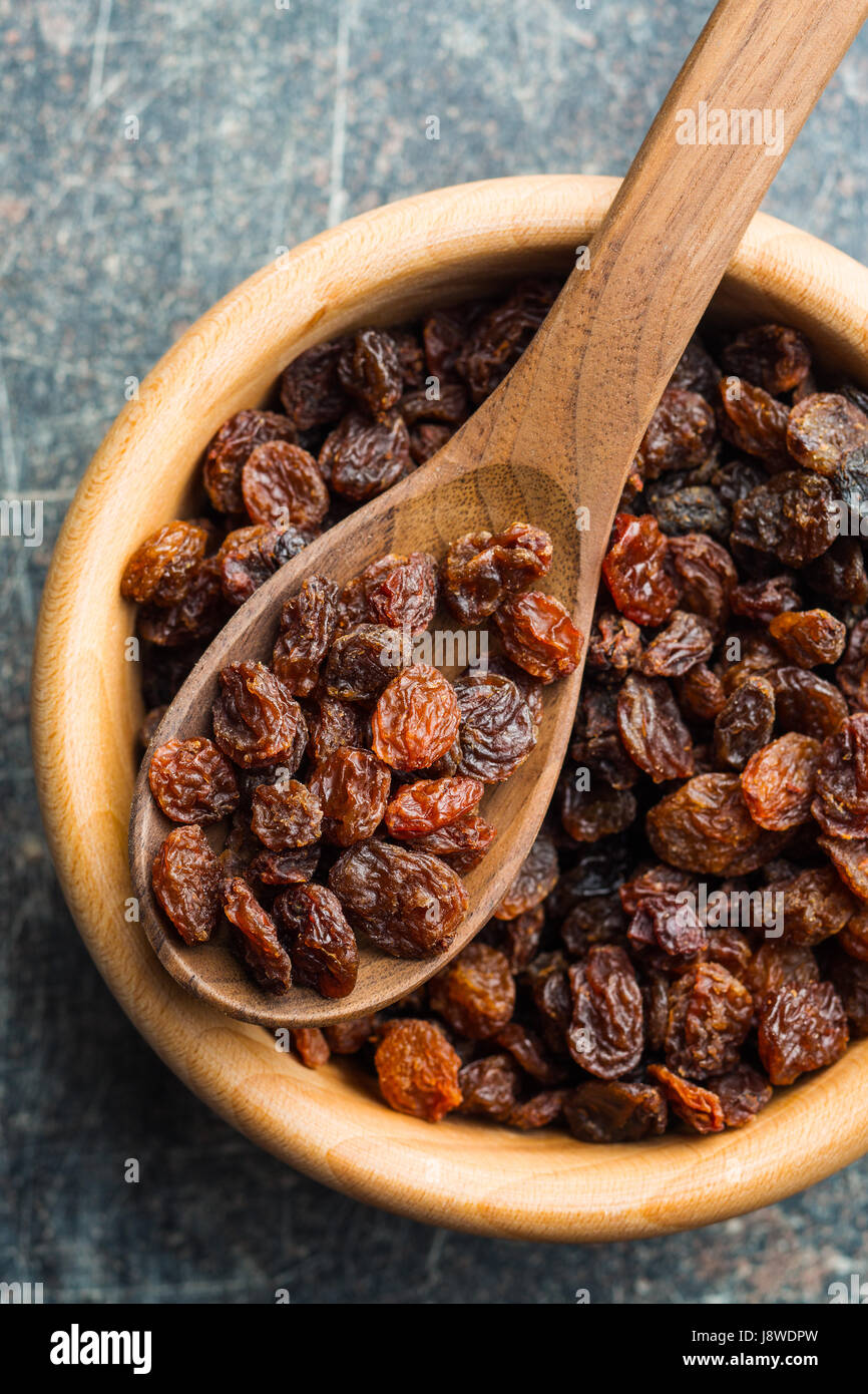 Sweet dried raisins in wooden spoon on old kitchen table. Top view ...