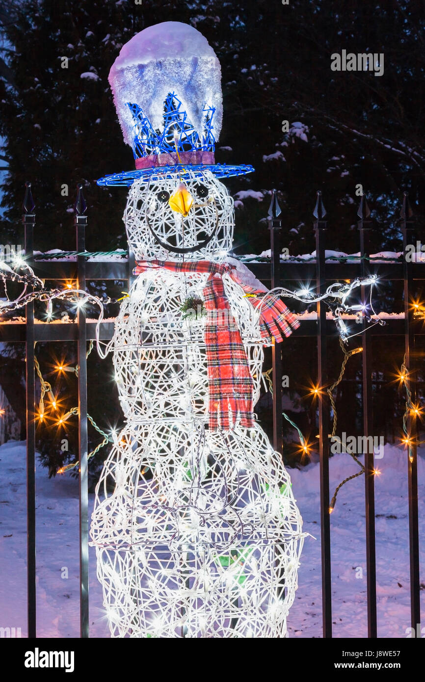 Illuminated decorative snowman attached to wrought iron fence at dusk ...