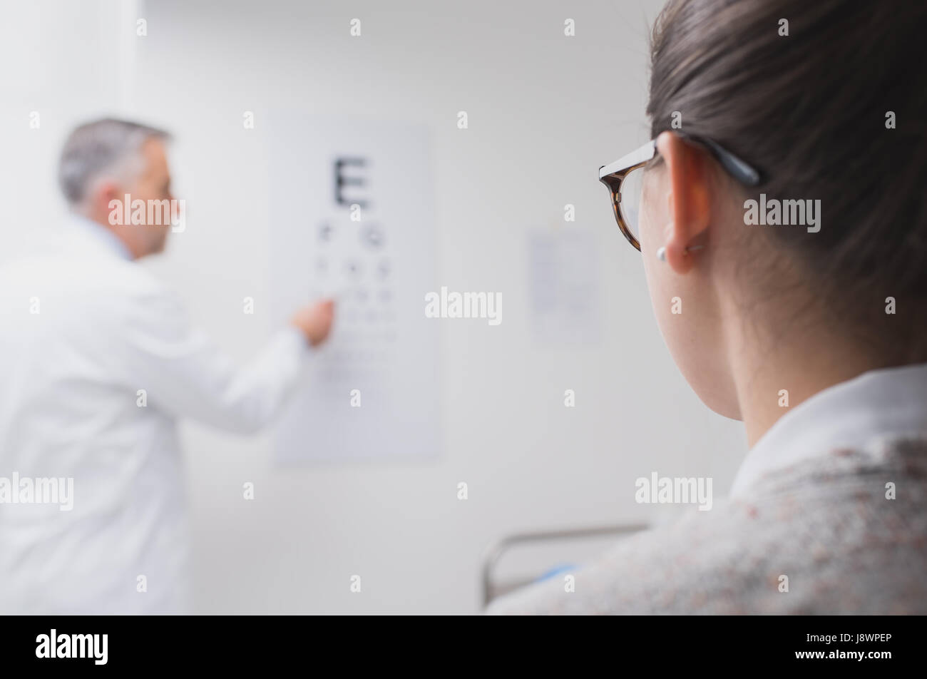 Woman reading the eye chart, the oculist is pointing at one letter and ...
