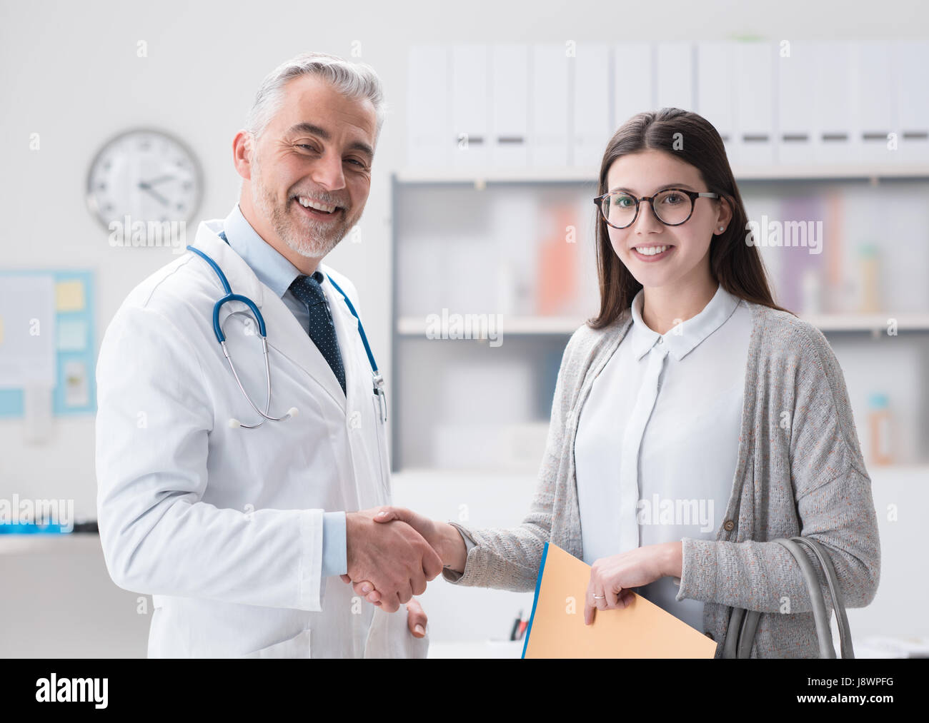 Smiling confident doctor shaking hands with a female patient in the ...