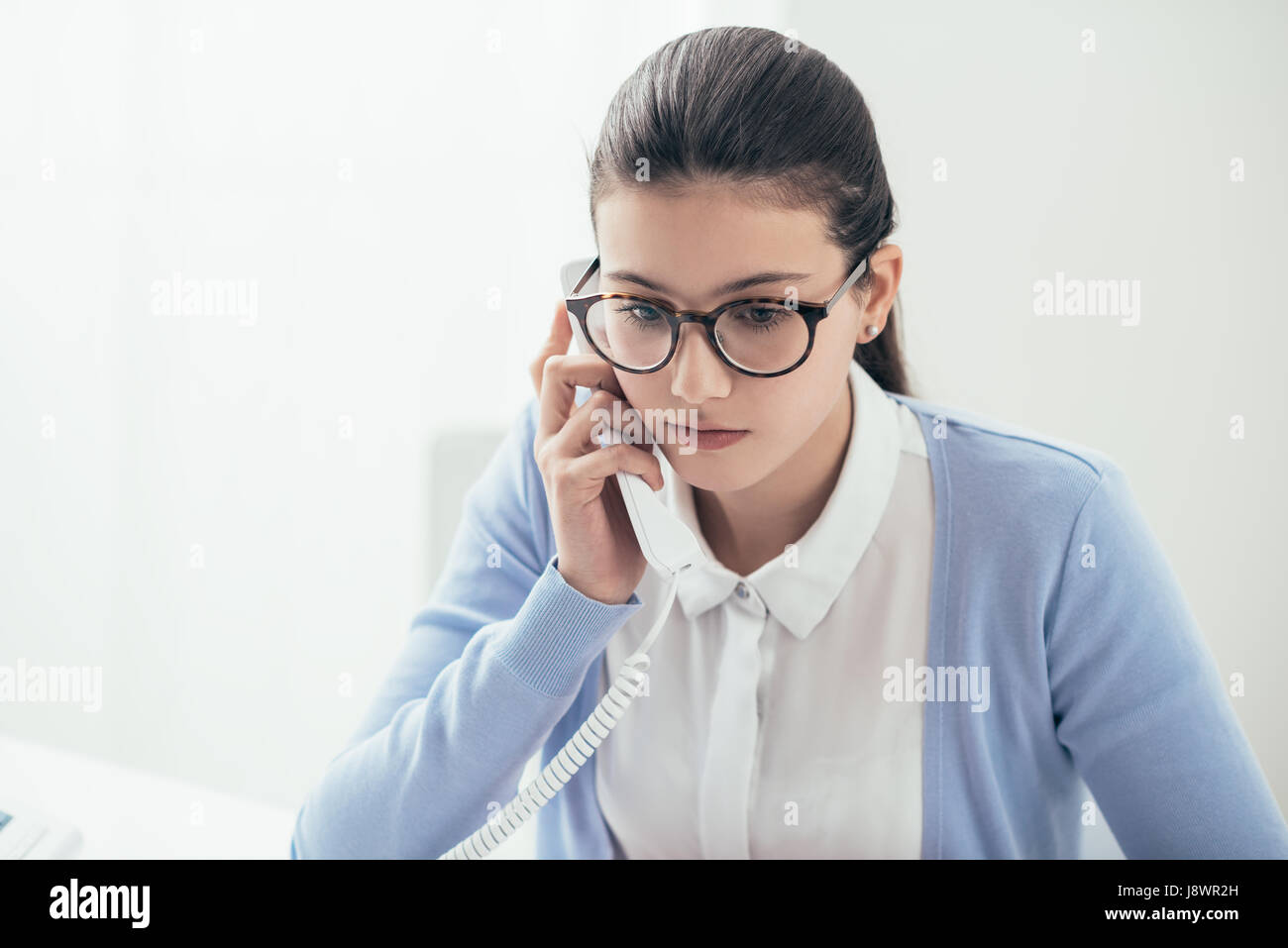 Young efficient secretary working in the office, she is answering phone ...