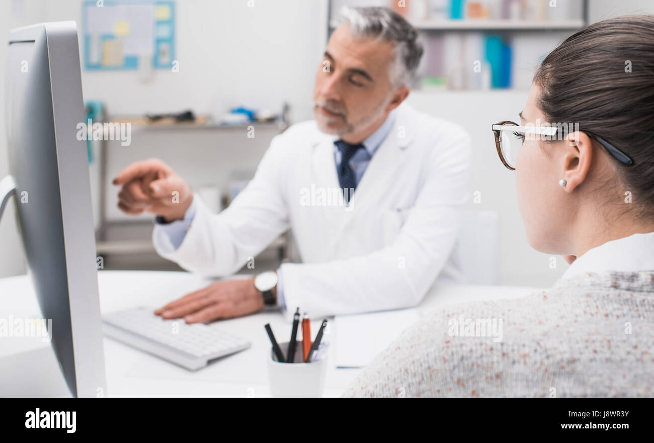 Doctor showing medical records on his computer to his patient, he is ...