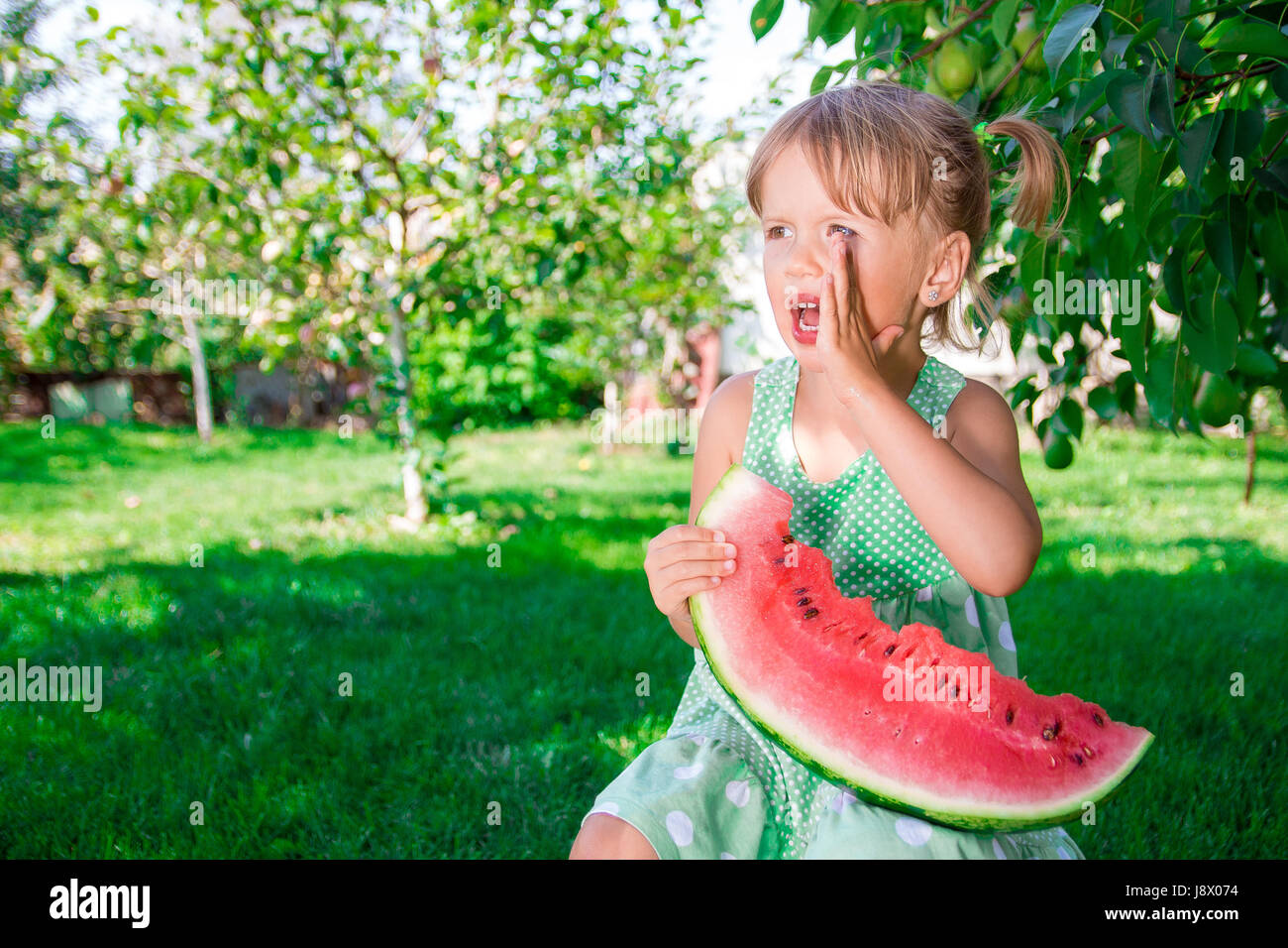 Little blonde with slice of watermelon in summer park. Happy. Screaming ...