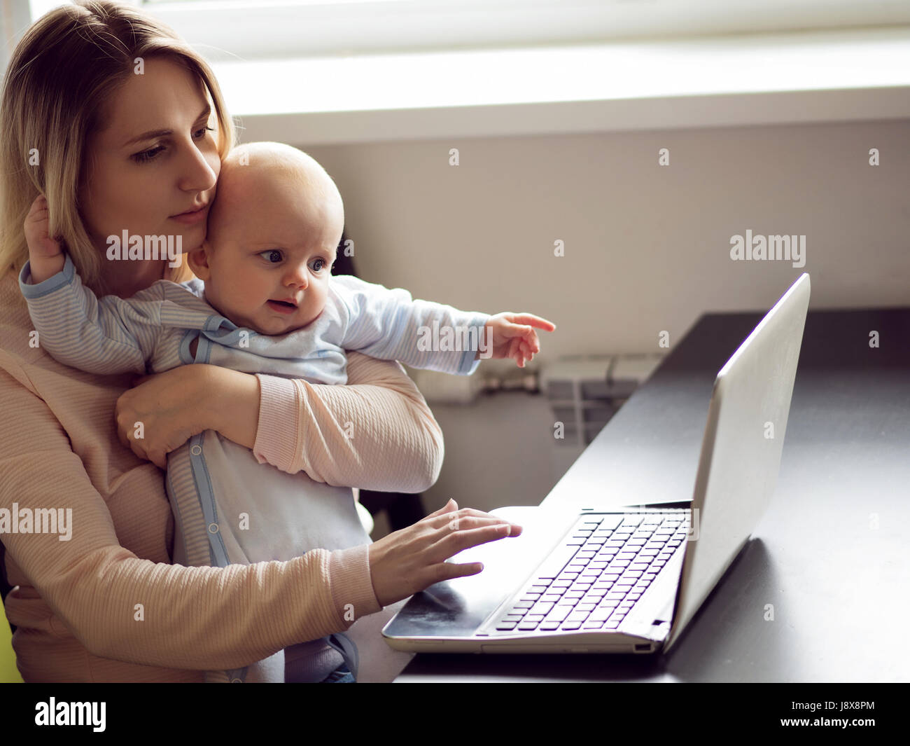 Young mother in home office with computer and her baby. Work and child ...