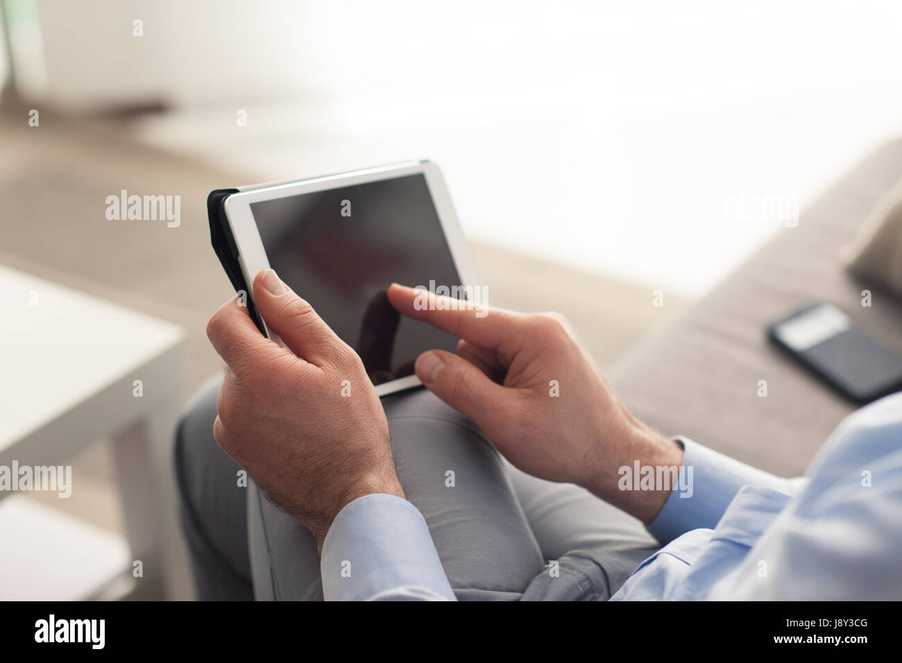 Man sitting on the couch and using a digital touch screen tablet, he is ...