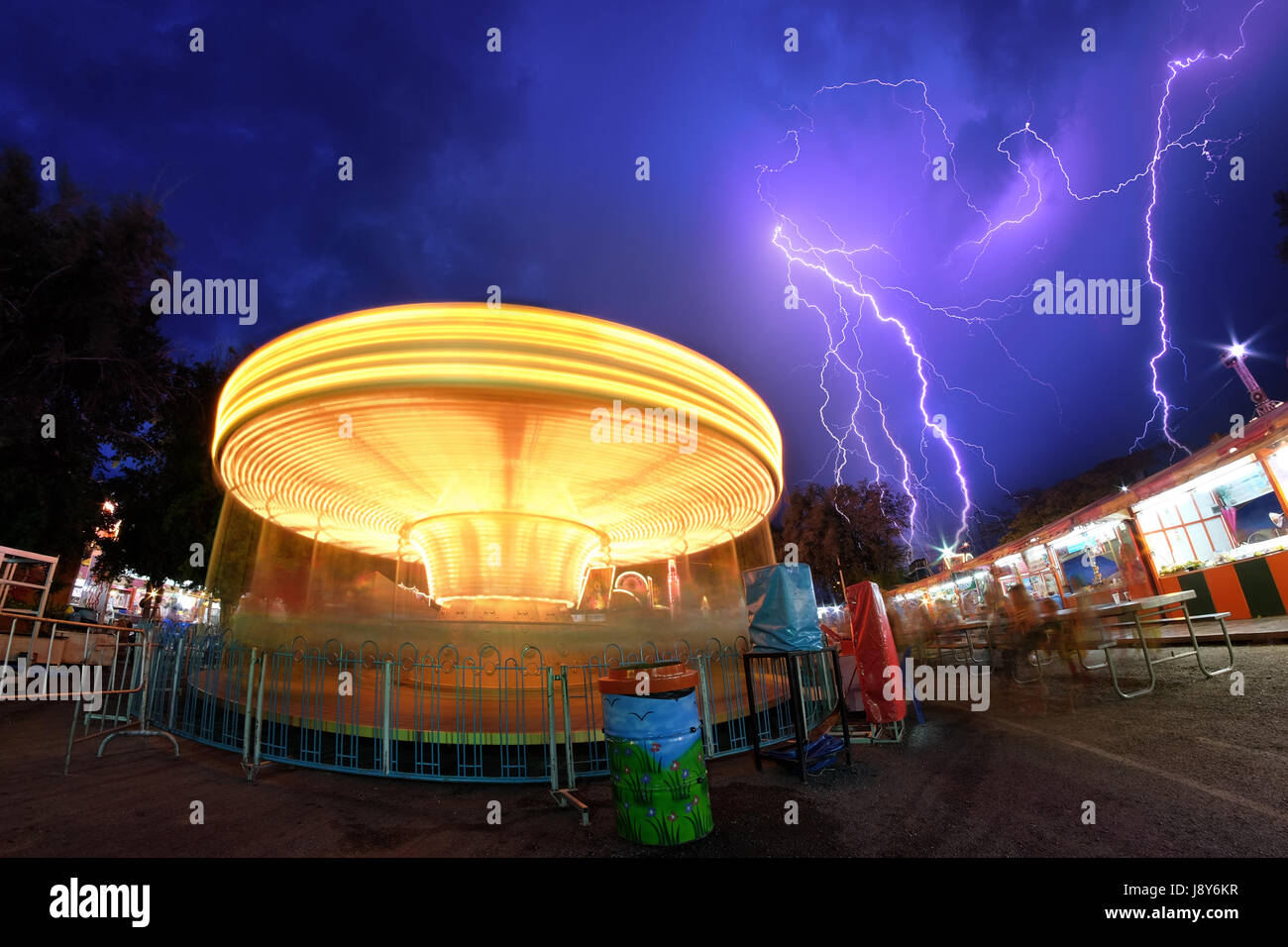 Colorful carousel in motion with thunderstorm in background, people ...