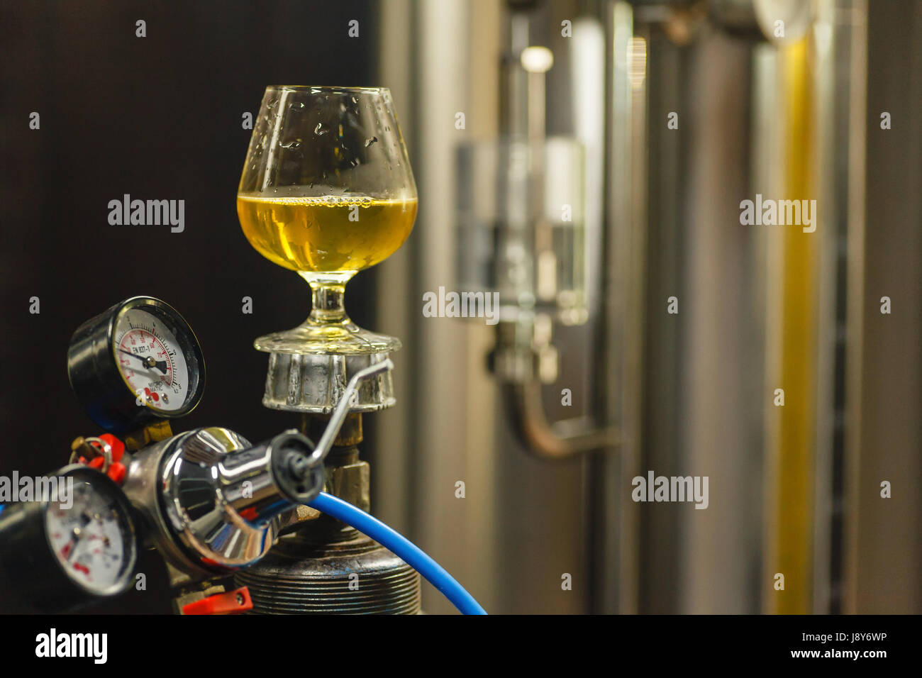 Tasting glass with clear lager beer standing on a gas tank at a brewery ...