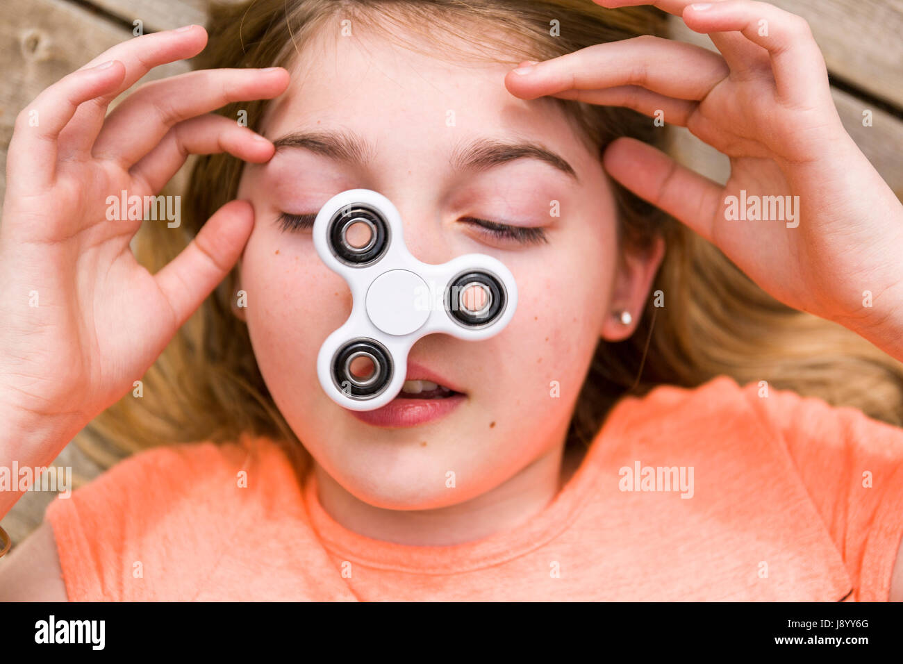 Female teenager playing with fidget spinner spinning toy on her nose ...