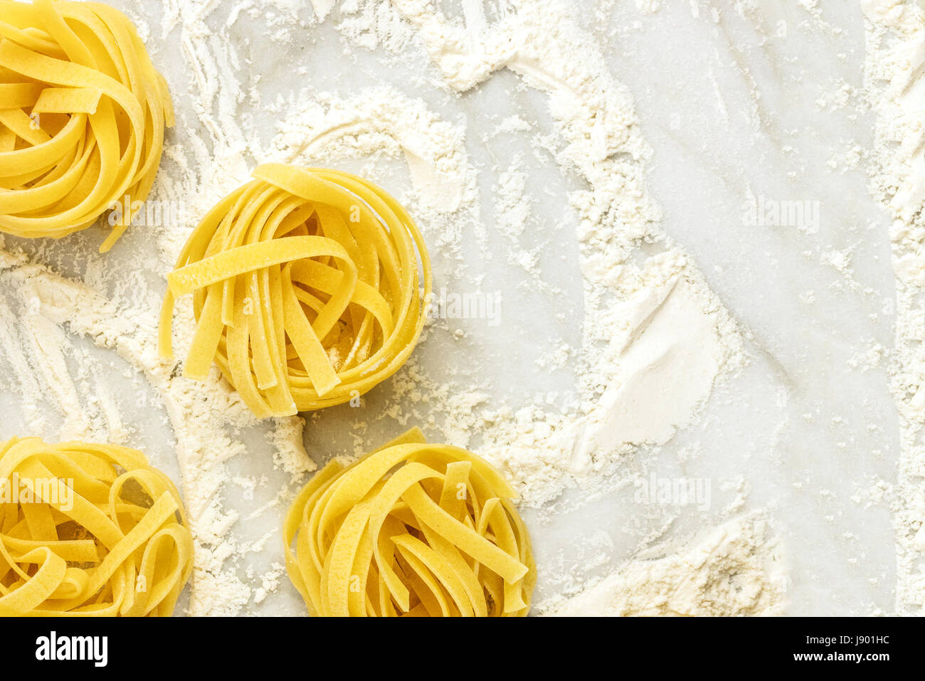 An overhead photo of pasta nests on a white marble table with flour and ...
