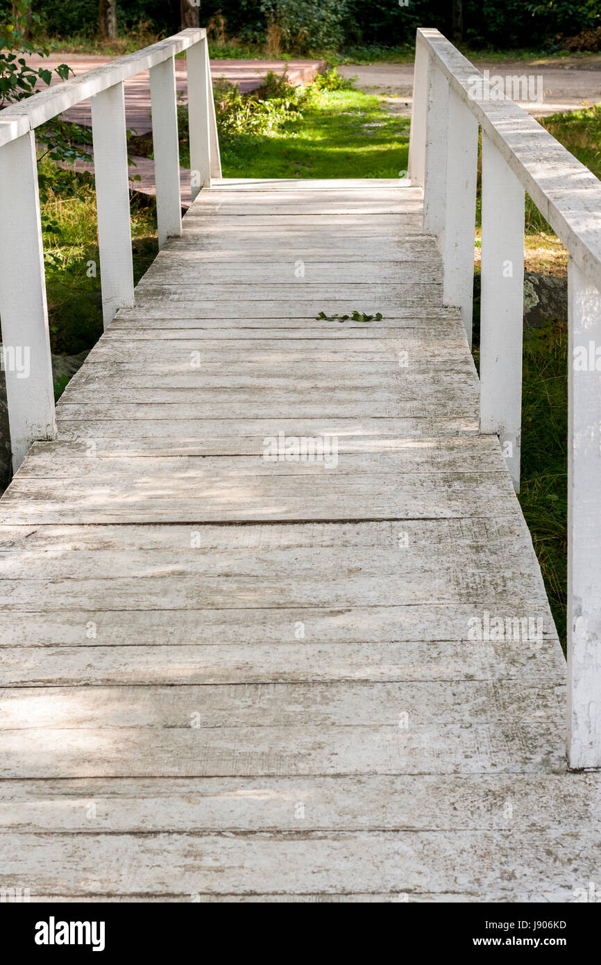 Old wooden painted white paint bridge in sunny summer forest. Retiring ...