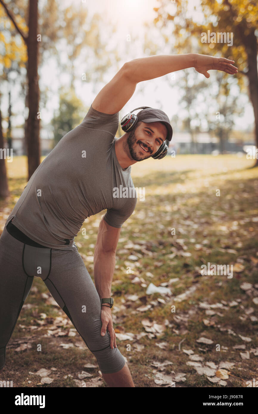 Young smiling sportsman with headphones doing stretching exercise in ...