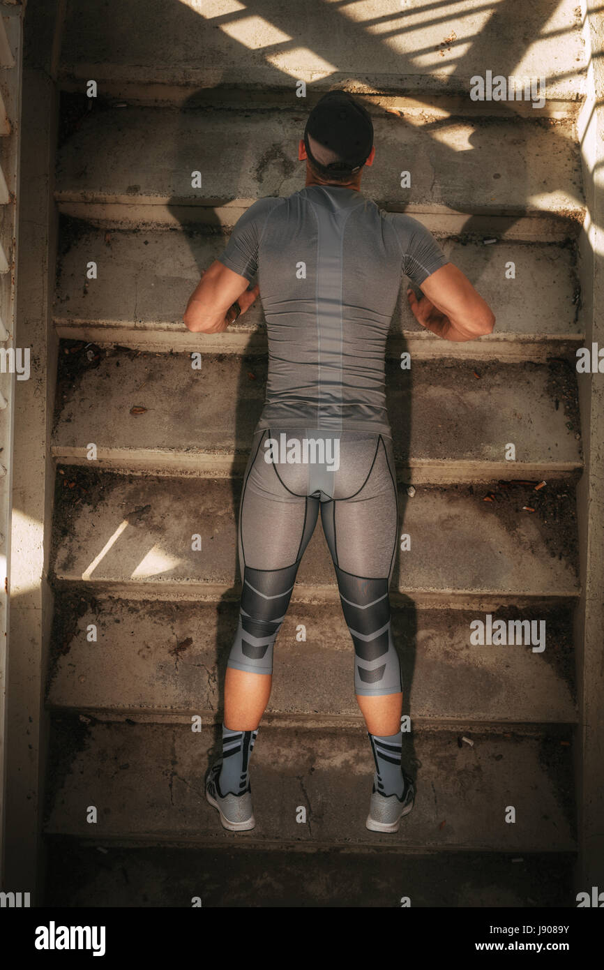 Young muscular sportsman doing push-up exercise on the stairs. Rear ...