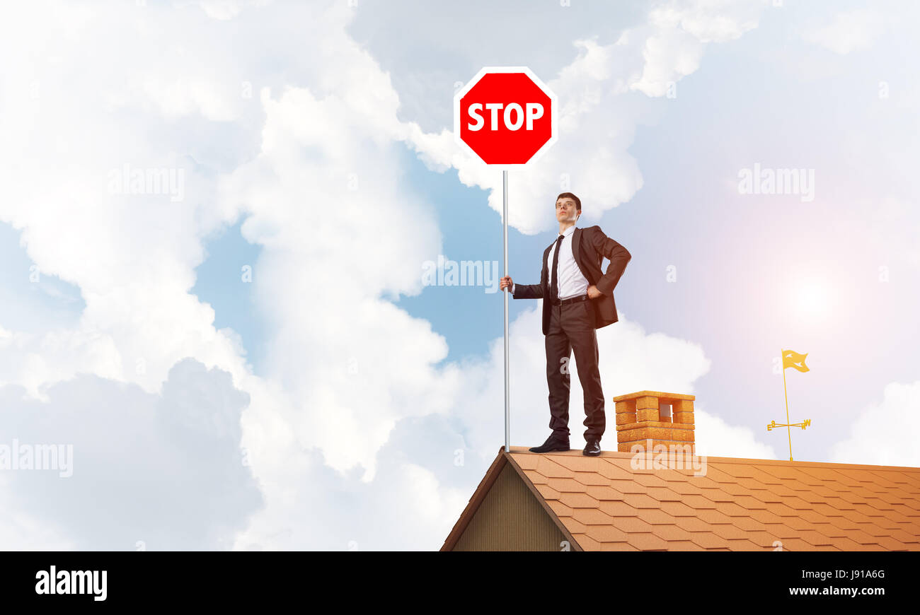 Caucasian businessman on brick house roof showing stop road sign. Mixed ...