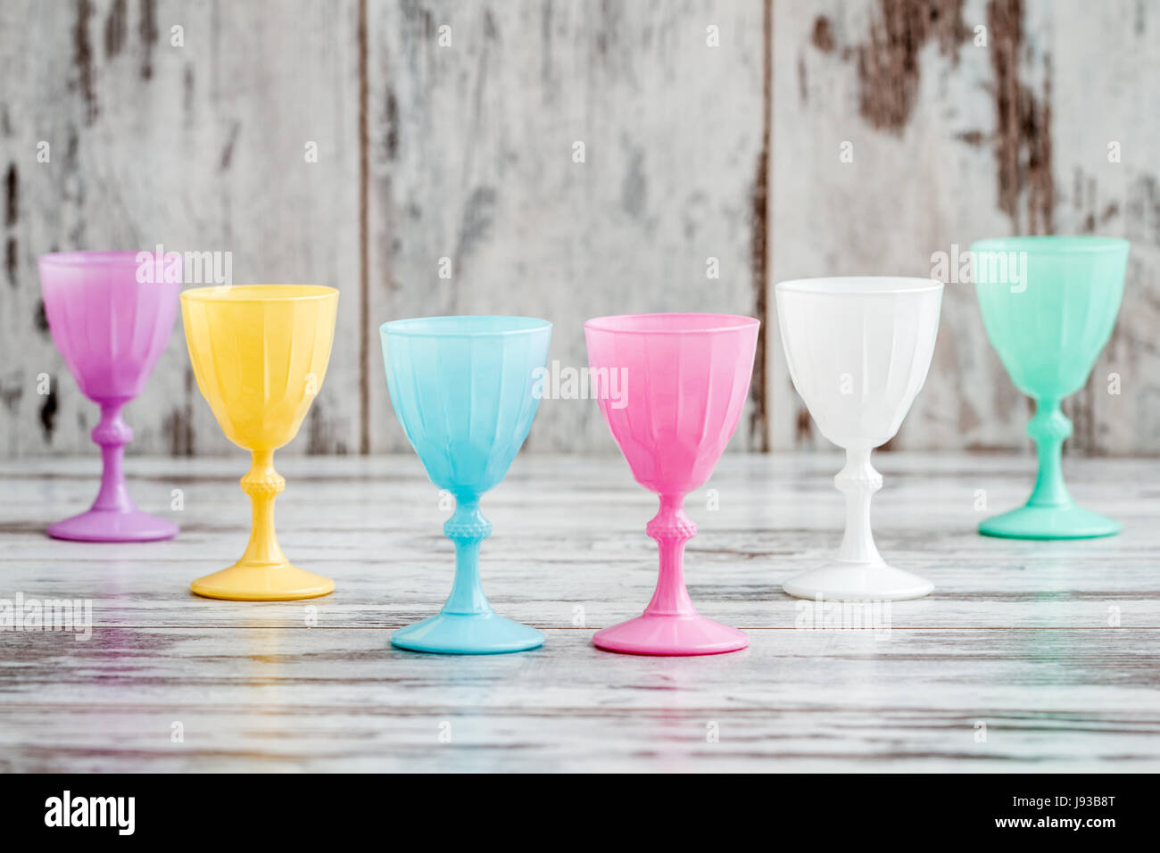 Row of multi colored glasses on white wooden background Stock Photo - Alamy