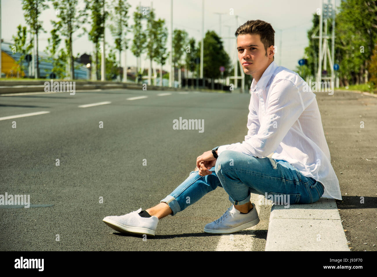 Attractive smiling man sitting by city street Stock Photo - Alamy