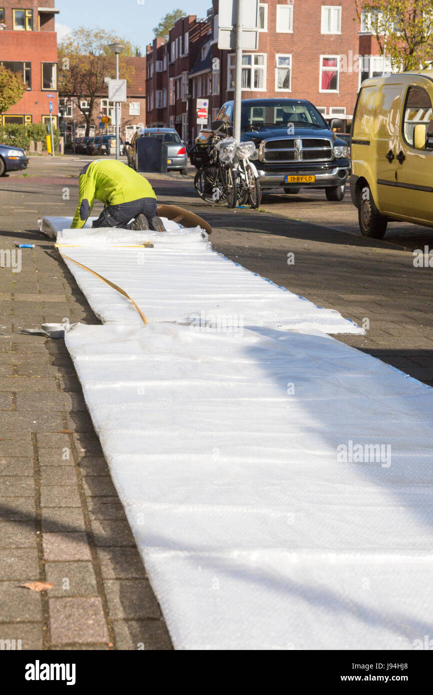 Worker cutting and taping insulation material on the street to be ready ...