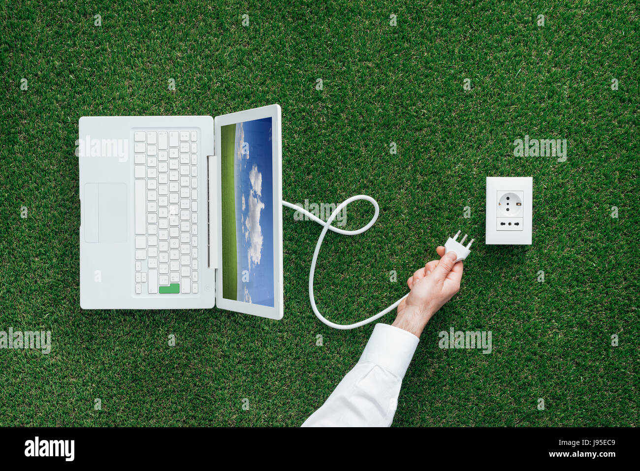 Man plugging a laptop into a socket on the grass, green renewable ...