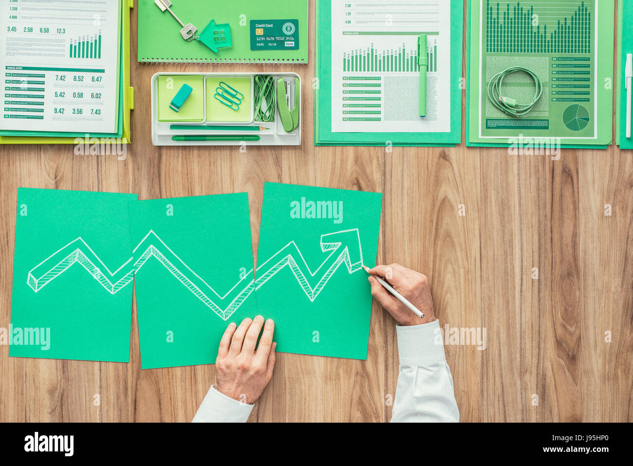 Businessman drawing a financial chart with arrow on green sheets ...