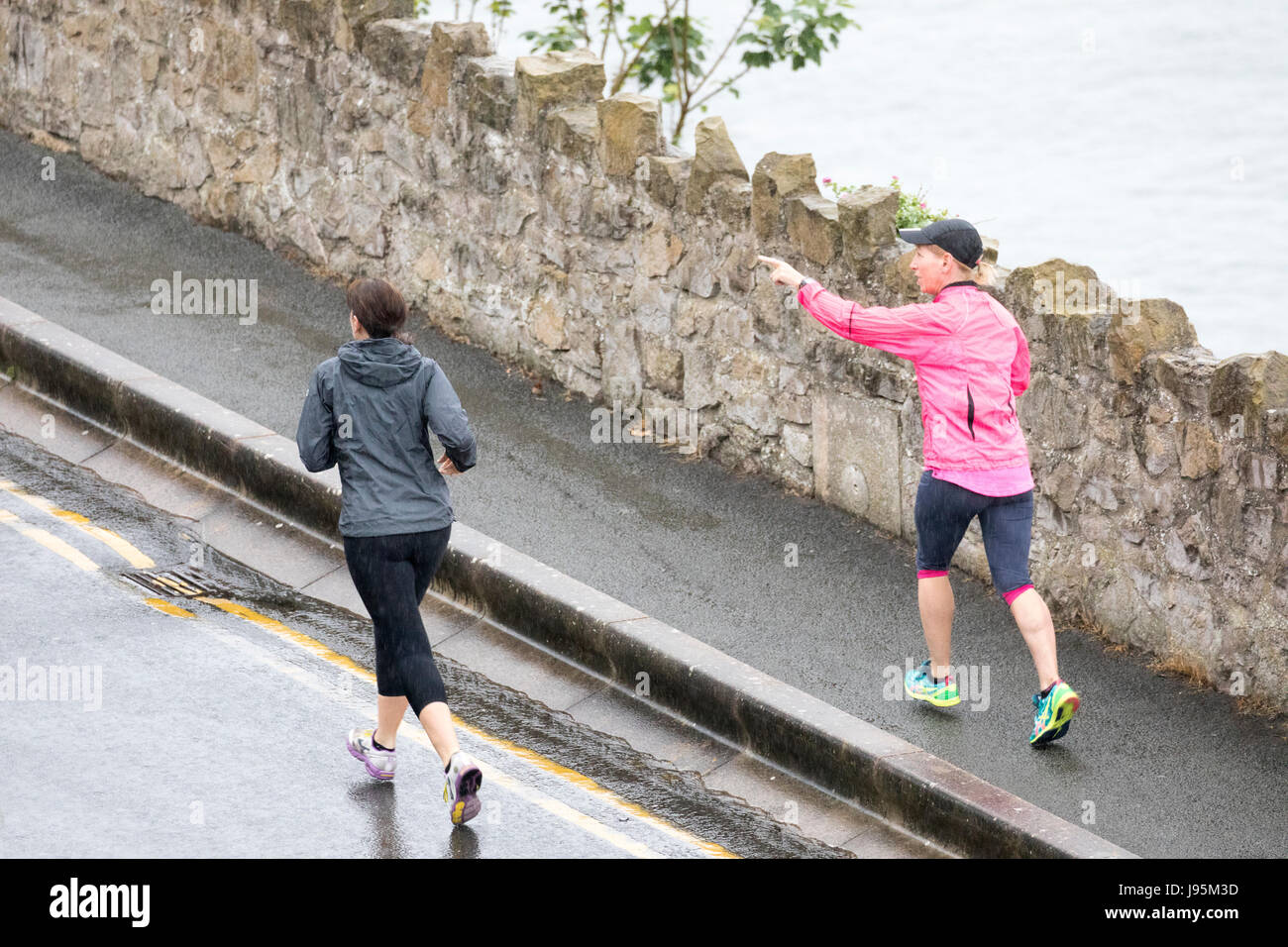 Two women jogging with one pointing as they jog along the coastal road ...