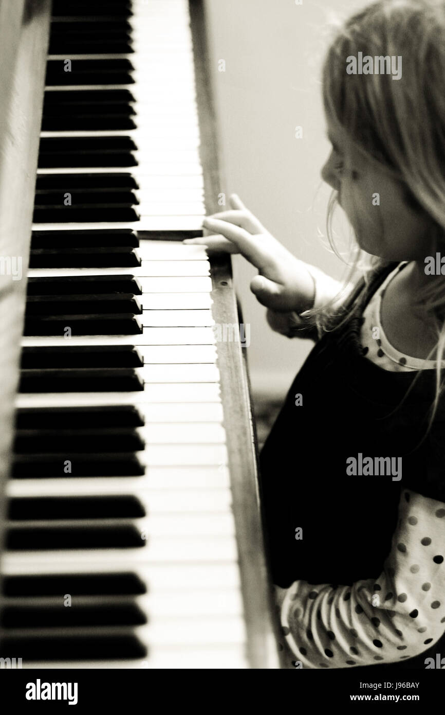 Side profile of a child with long hair sitting at a piano playing a ...