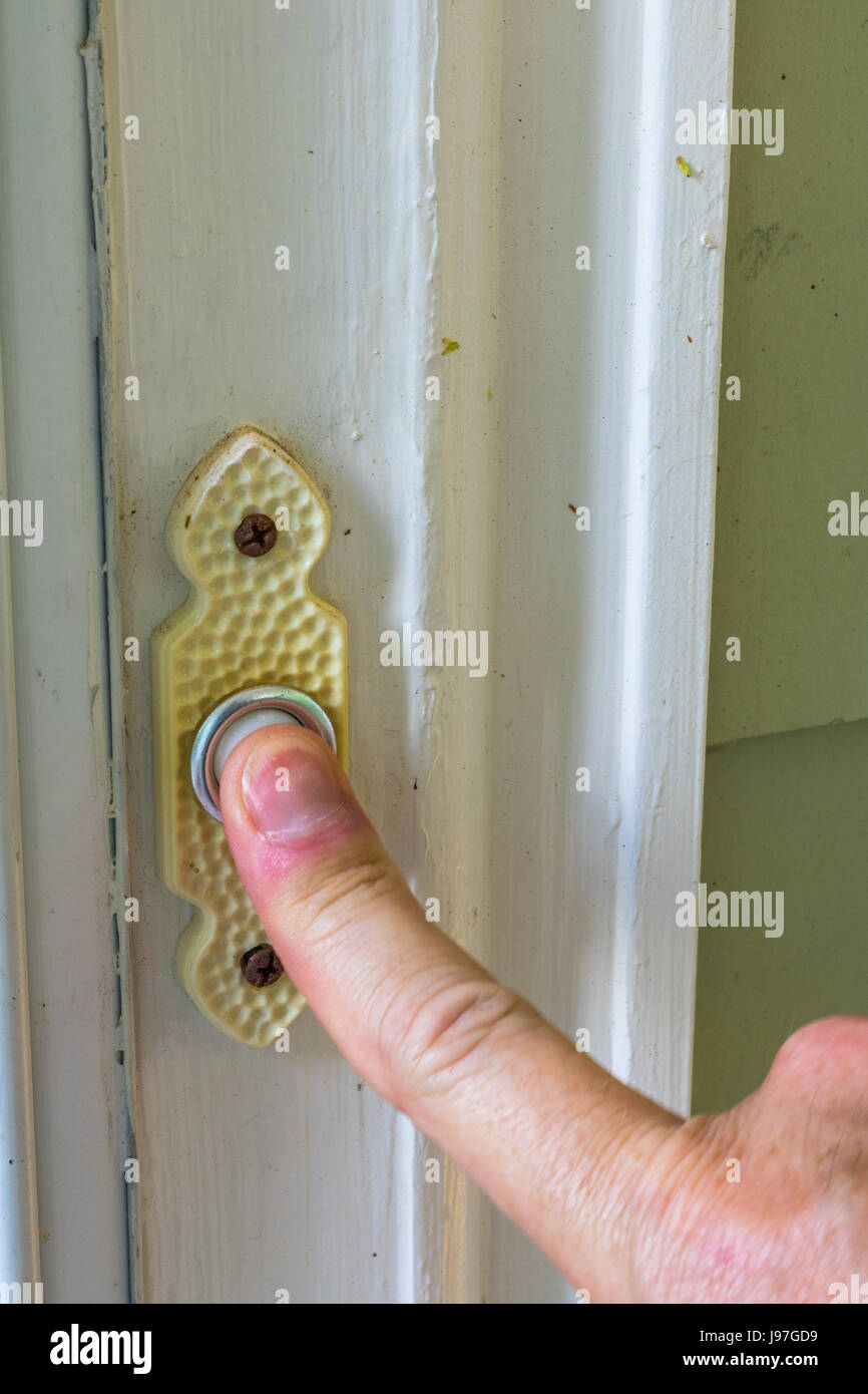 Male finger ringing a doorbell to a front door with a white frame on a ...
