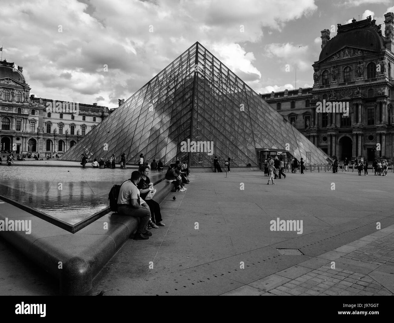 La Louvre from the front with people sitting down. View is of the ...