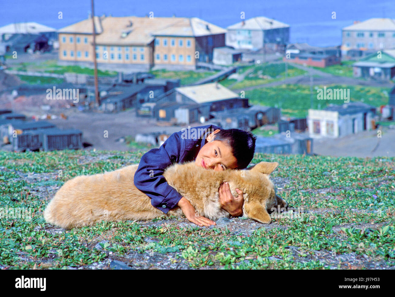 Russian Yupik boy and his dog playing on hillside above Yupik village ...