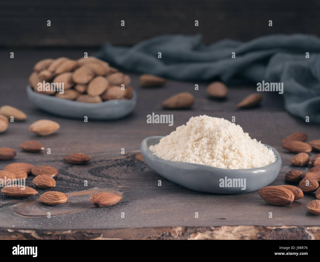 Almond powder in gray trendy plate and almonds on dark wooden table ...