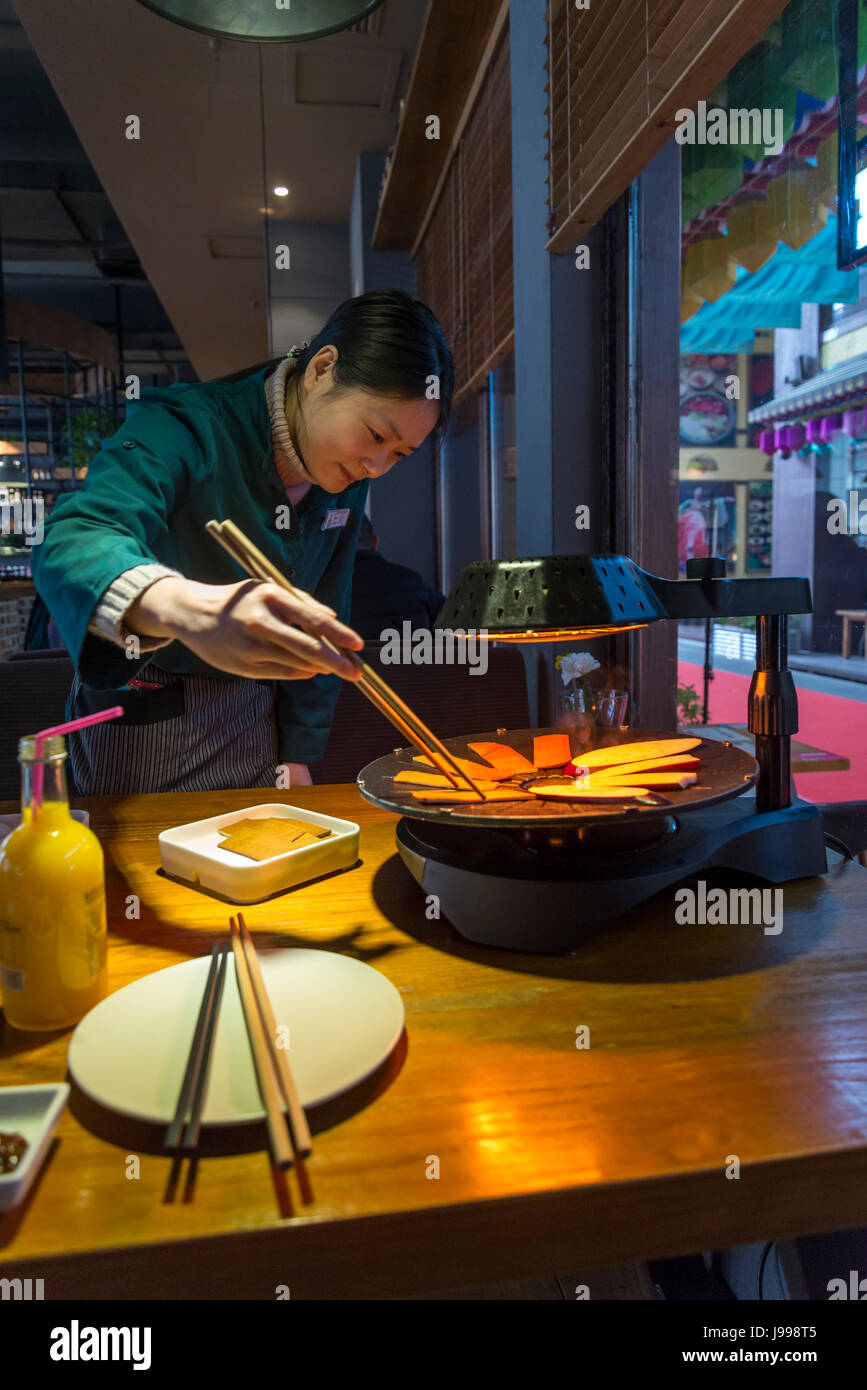 Waitress cooking vegetables for a guest on Chinese Infrared electric ...