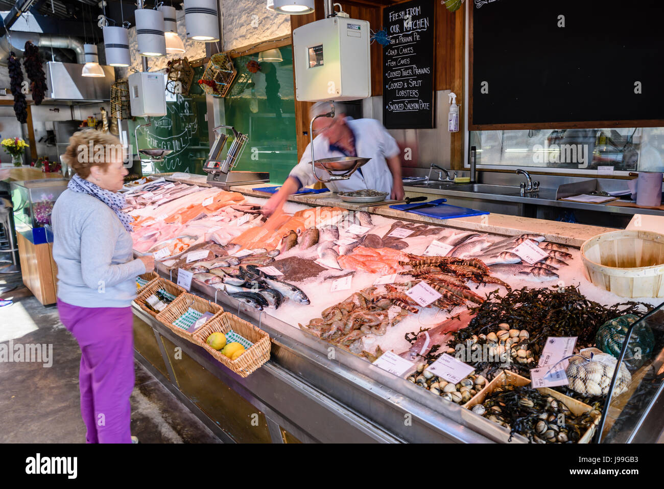 A fishmonger lifts fish from a large counter stocked with lots of fresh ...