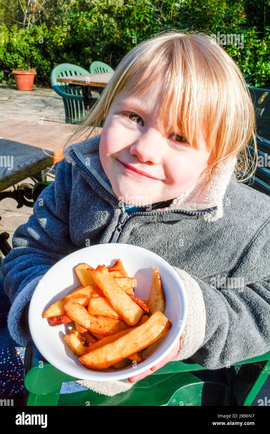 Cute five year old girl eating chips from a bowl in an outdoor cafe ...