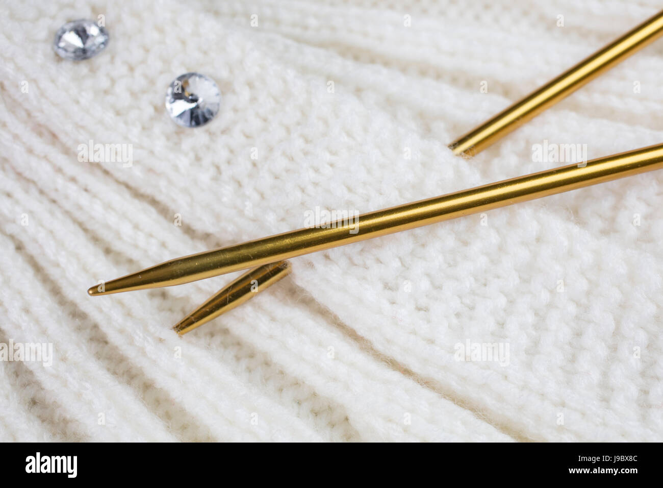 White yarn knitted garment with gold colored knitting needles Stock ...