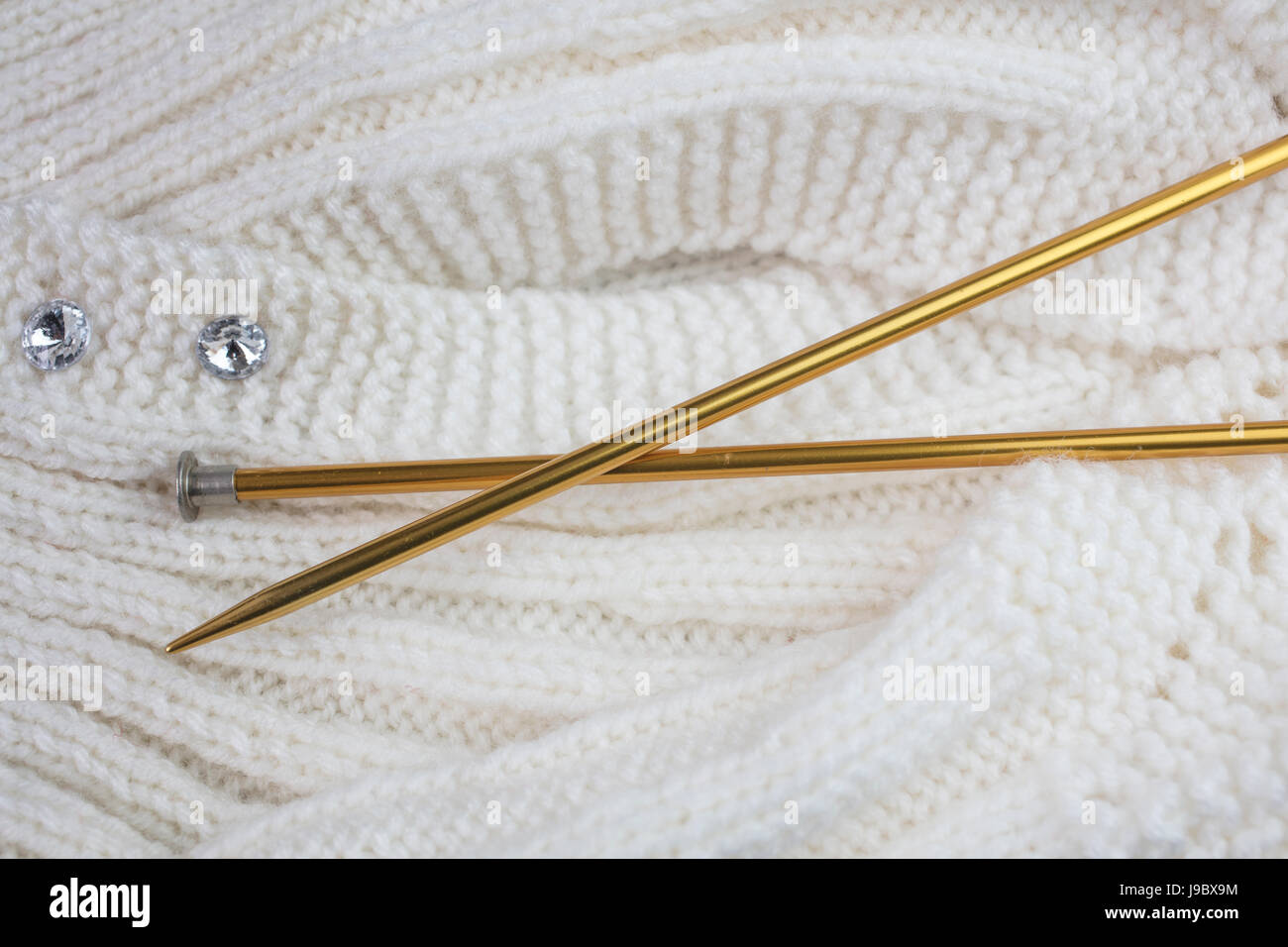 White yarn knitted garment with gold colored knitting needles Stock ...