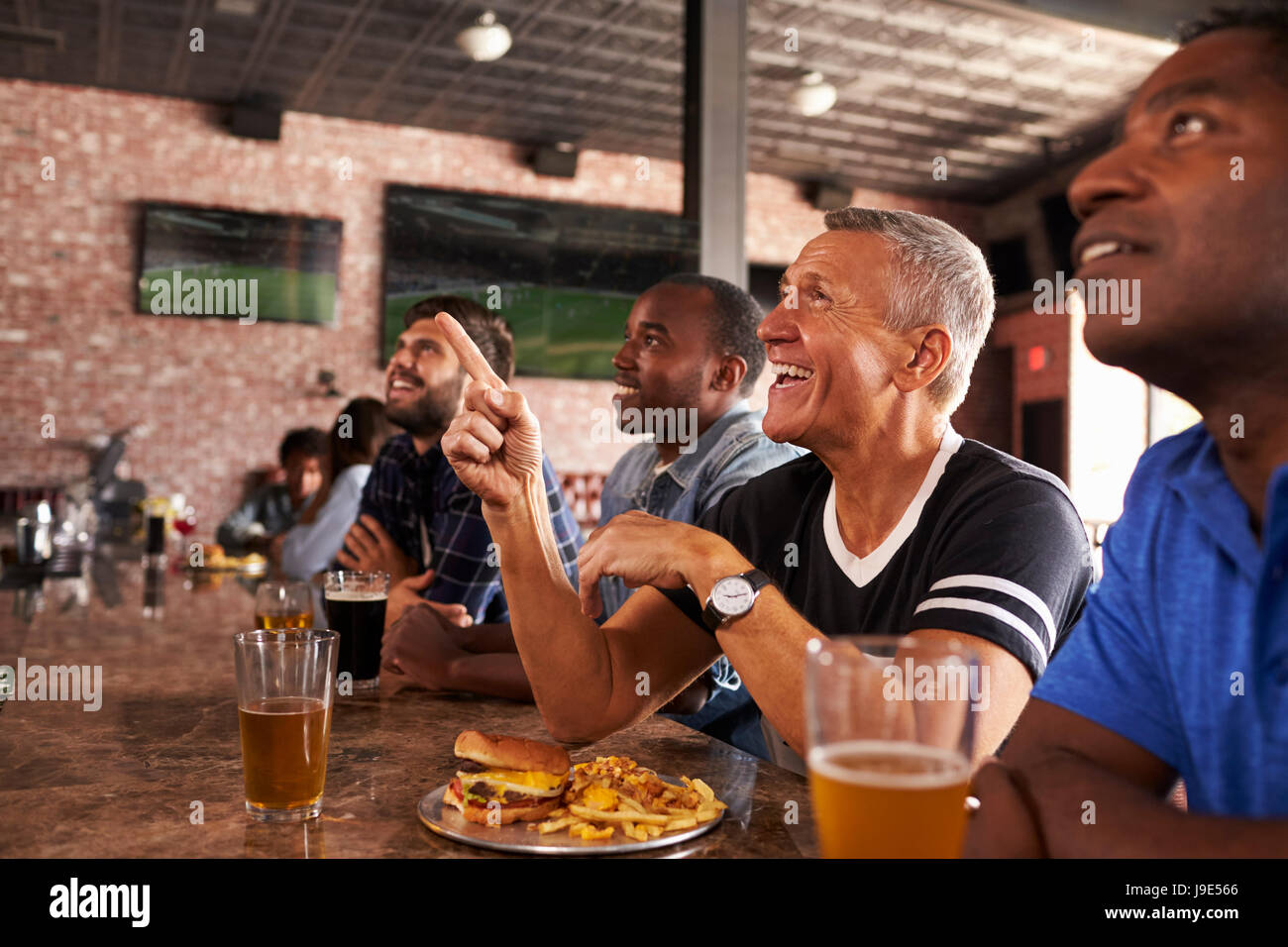 Male Friends At Counter In Sports Bar Watching Game Stock Photo - Alamy