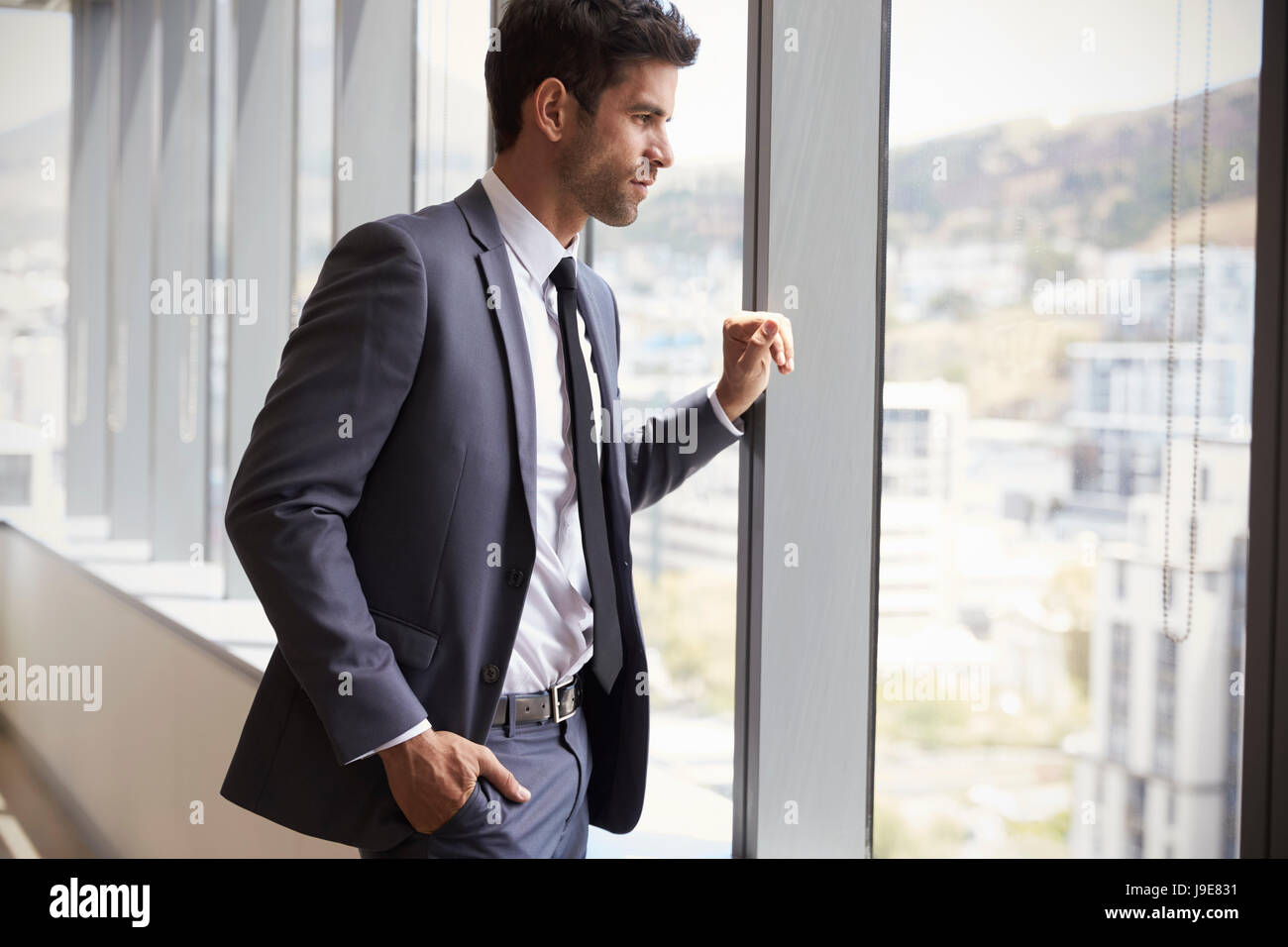 Young Businessman Looking Out Of Window In Office Stock Photo - Alamy