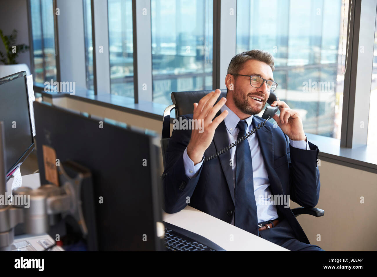 Businessman Making Phone Call Sitting At Desk In Office Stock Photo - Alamy