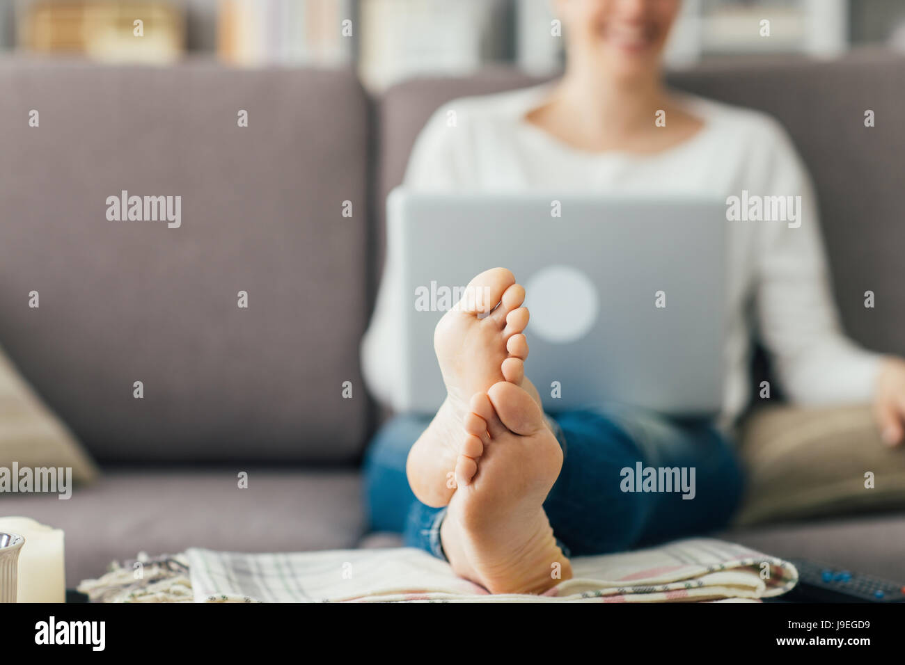 Young woman at home relaxing on the couch, she is using a laptop, feet ...