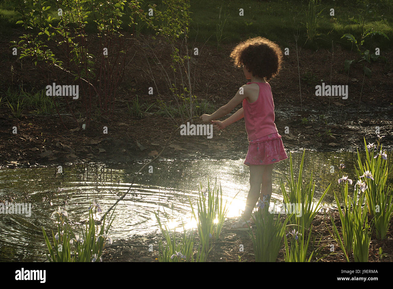 Little cute girl playing with stick in small pond Stock Photo - Alamy