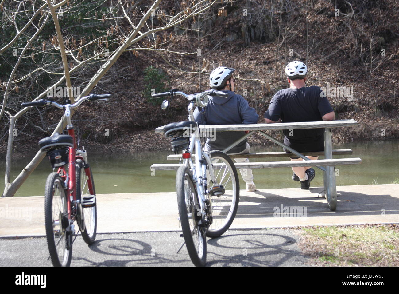 Two adult men resting on bench by the river after bike ride Stock Photo ...