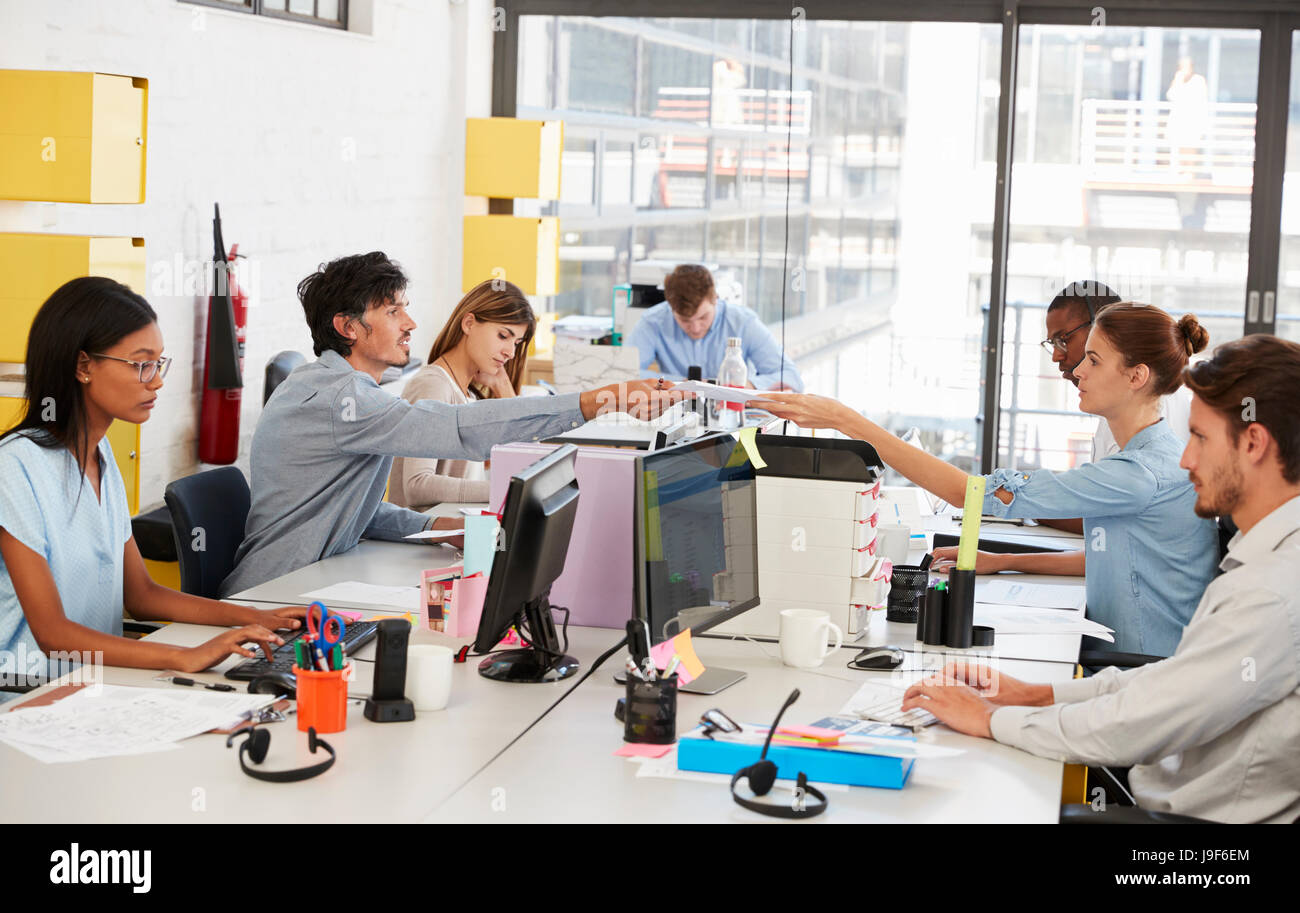 Colleagues passing paperwork across desk in a busy office Stock Photo ...
