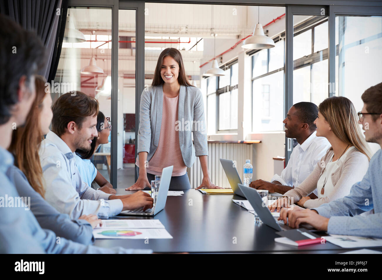 Woman addressing team leans on desk at business meeting Stock Photo - Alamy